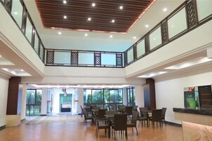 Um hall amplo com pé direito alto, área central aberta com mesas e cadeiras, e grandes janelas que oferecem iluminação natural.