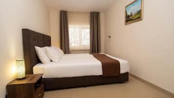 Quarto com cama, mesa de cabeceira com abajur, janela com cortinas e um quadro na parede.