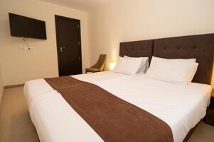 Quarto de hotel com uma cama grande, televisão de tela plana na parede, uma porta e uma cadeira.