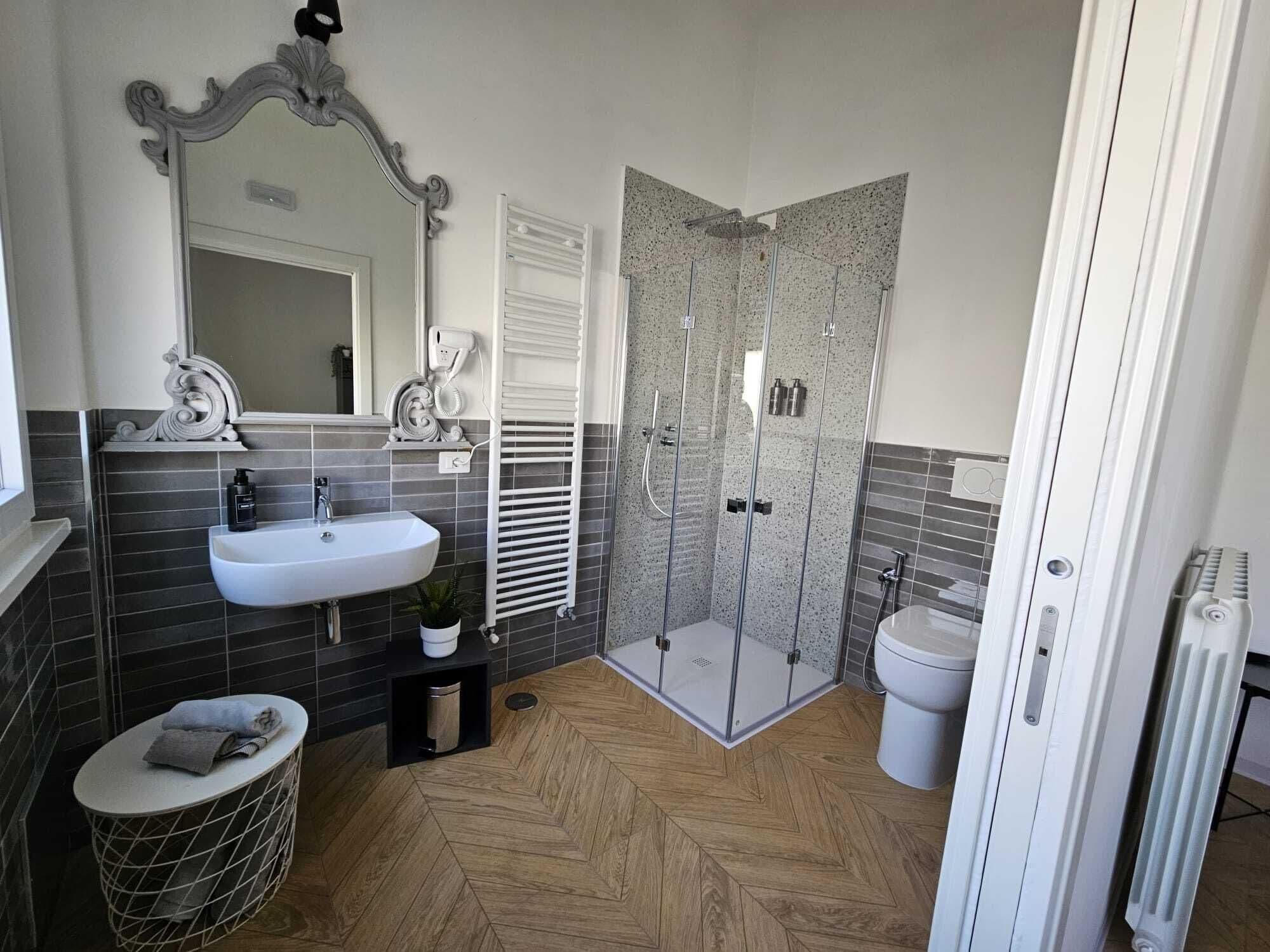 Casa de banho com lavatório branco, espelho, cabine de duche e sanita.