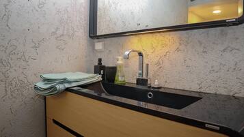 Casa de banho moderna com lavatório preto, espelho e pilha de toalhas.