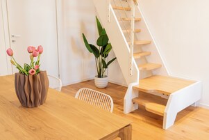 Um interior moderno com uma mesa de jantar de madeira, uma cadeira branca, uma planta em vaso e uma escada branca.