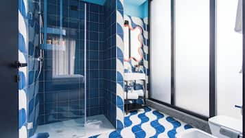 Uma casa de banho com azulejos estampados em azul e branco, zona de duche separada por vidro, lavatório branco e sanita.