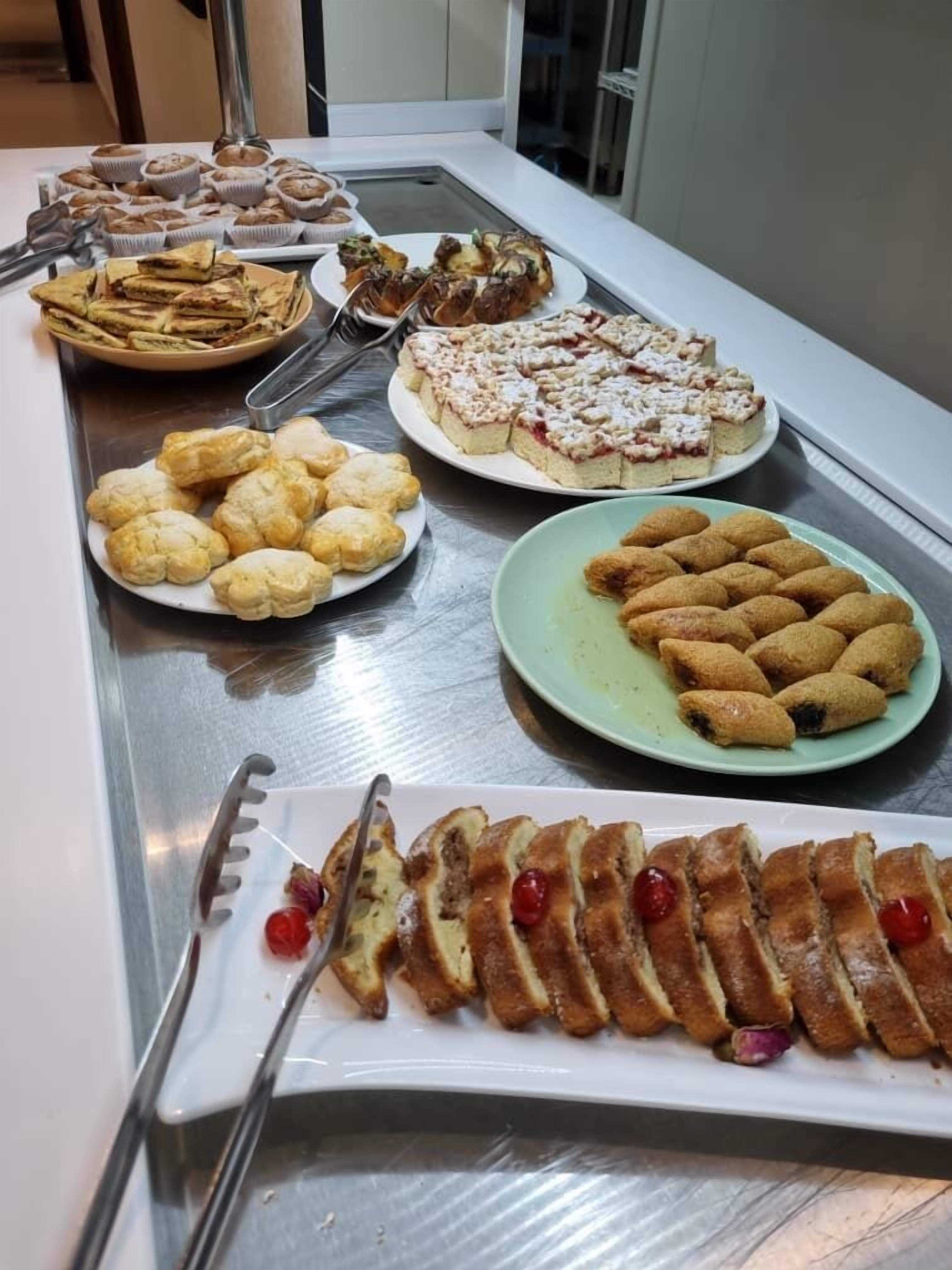 Um buffet com diversos pastéis e sobremesas, incluindo scones, muffins e um bolo com cobertura de cereja.
