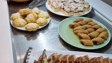 Um buffet com diversos pastéis e sobremesas, incluindo scones, muffins e um bolo com cobertura de cereja.