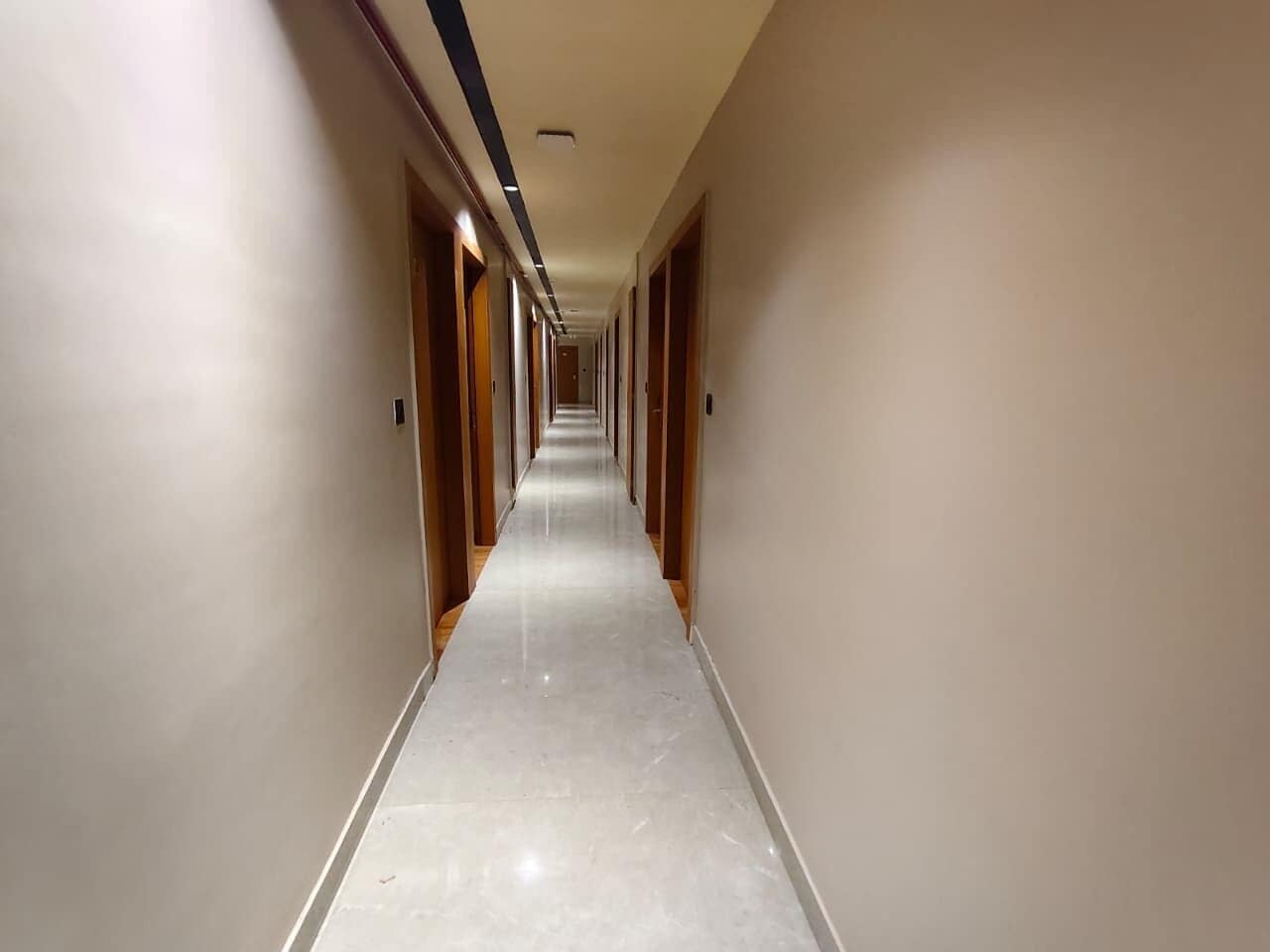 Um corredor comprido e estreito, com portas de madeira em ambos os lados e um chão brilhante e refletor.