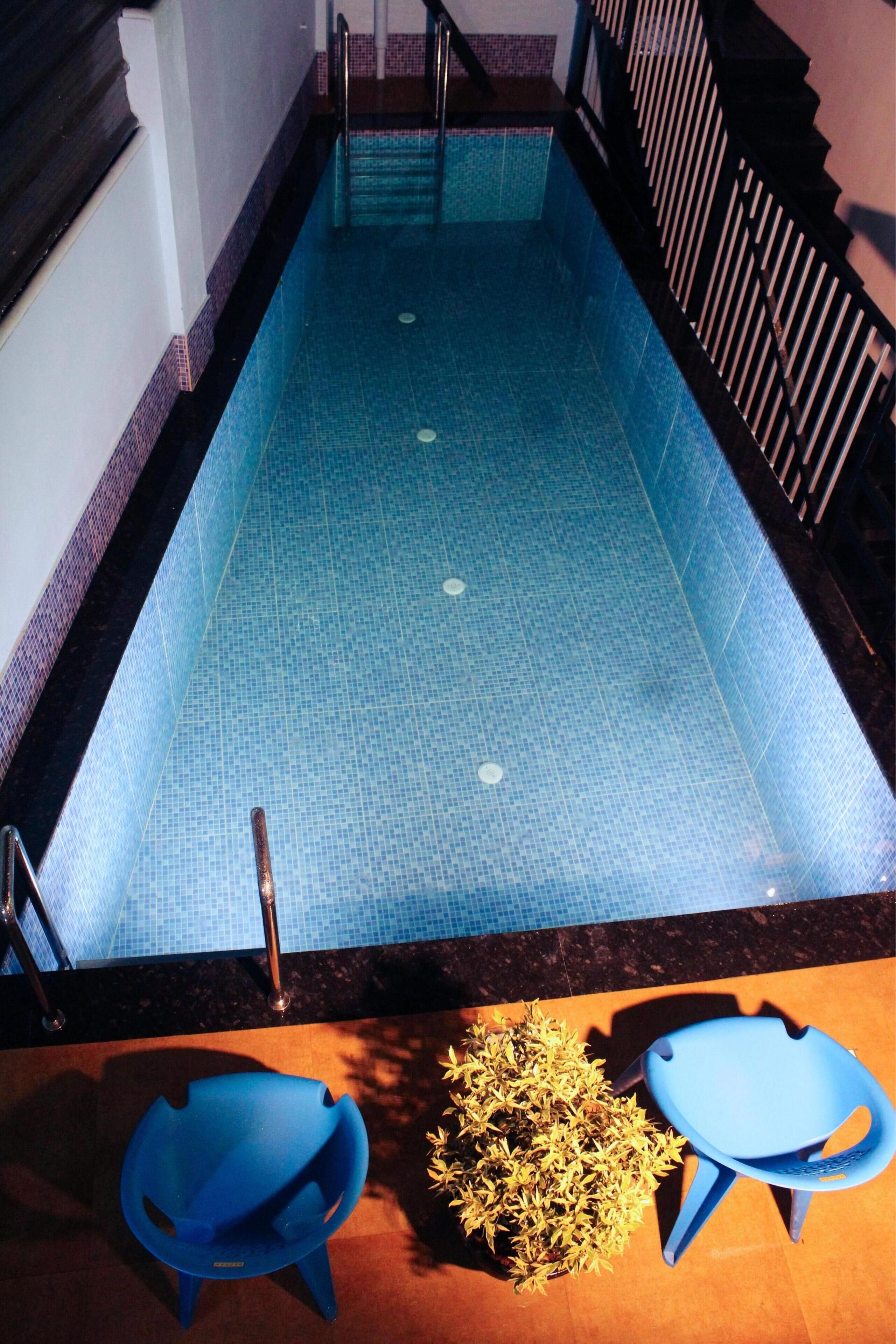 Uma piscina com piso revestido, uma escada de metal e duas cadeiras azuis.