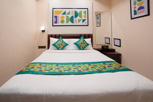 Quarto de hotel com cama bem arrumada, cabeceira, mesa de cabeceira e luminária na parede.