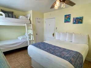 Um quarto com beliches, uma escada, uma cama com cobertor estampado e duas pinturas na parede.