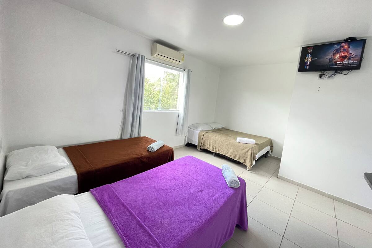 Quarto de hotel com duas camas, janela com cortinas, ar condicionado e televisão na parede.
