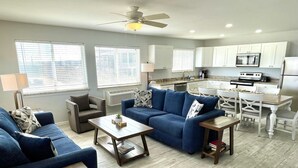 Uma sala de estar moderna com sofá azul, mesa de centro de madeira e área de jantar com cadeiras brancas.