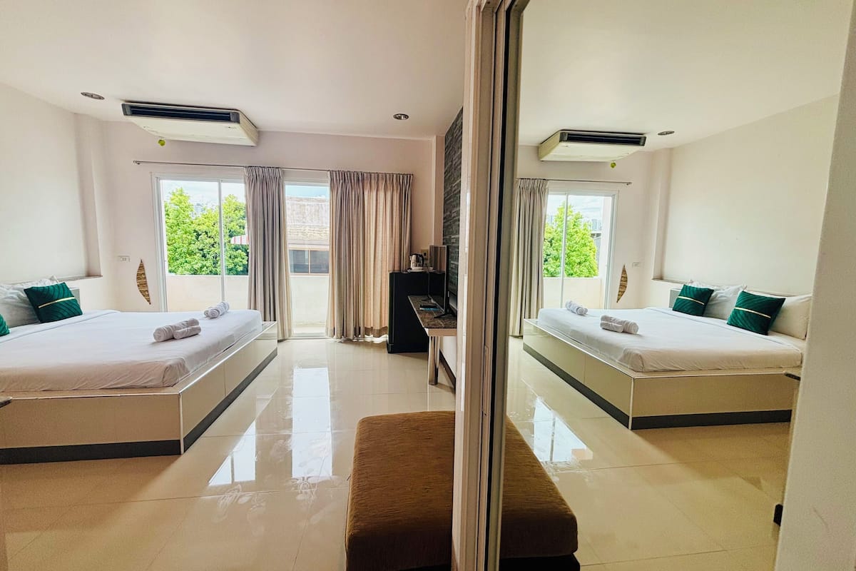 Quarto de hotel com duas camas, uma secretária pequena e vista para o verde lá fora.