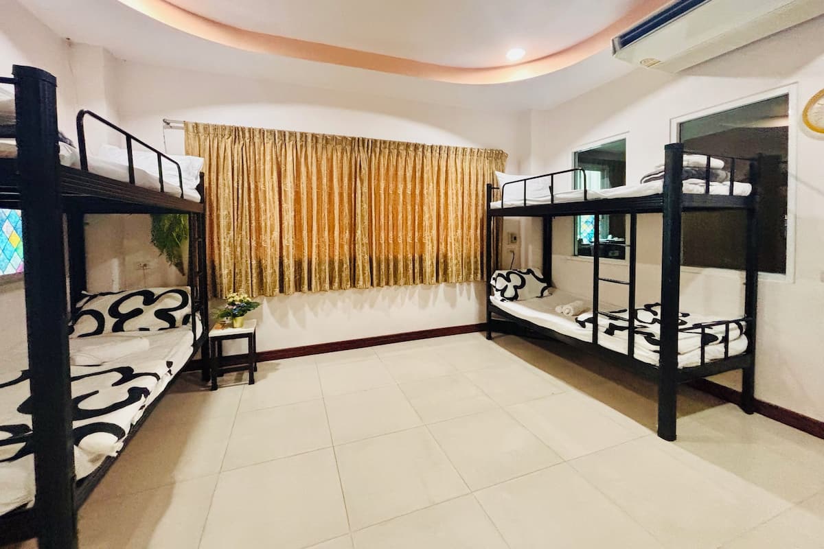 Quarto com beliches, uma mesinha com uma planta e uma janela com cortinas.