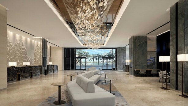 Um lobby moderno com um sofá seccional branco, um tapete estampado, um candelabro e vista para palmeiras através de grandes janelas.