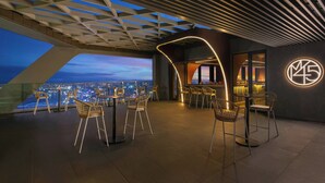Um bar no terraço com mesas e cadeiras, vista para a cidade e um design de teto marcante.