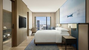 Quarto de hotel moderno com uma cama grande, uma TV de tela plana, uma escrivaninha e vista para a cidade através de uma janela ampla.