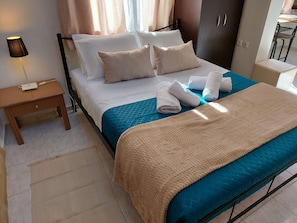 Uma cama bem arrumada com almofadas brancas e bege, um espalha-manta acolchoado verde-água e toalhas enroladas ao lado.