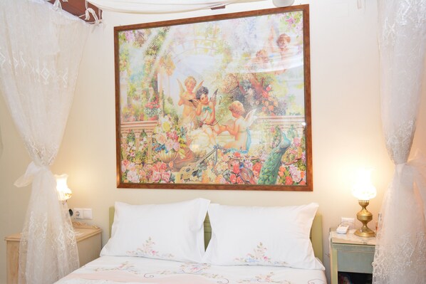 Quarto com pintura floral, cama com roupa de cama florida, mesa de cabeceira com abajur e criado-mudo com telefone.
