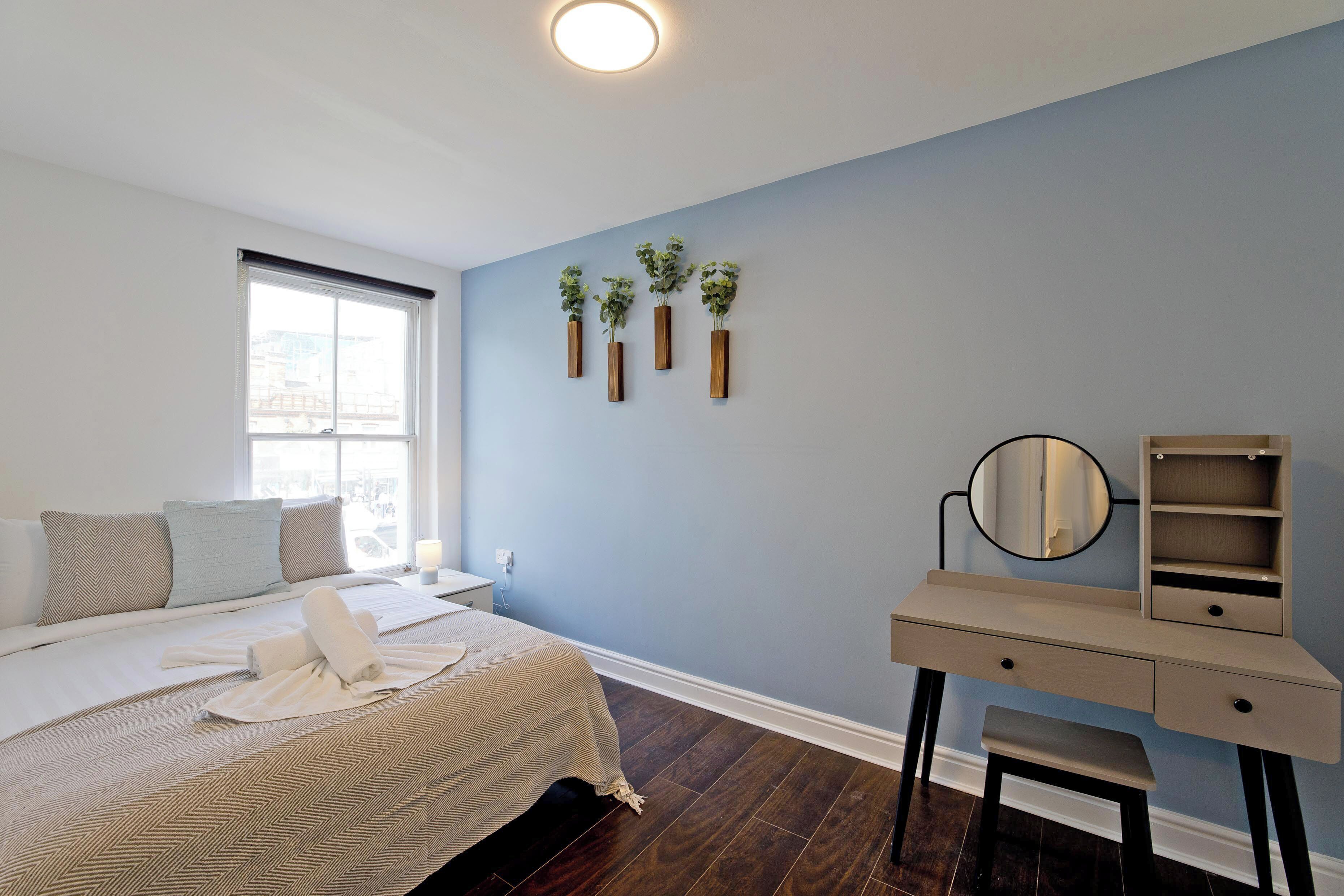 Quarto com cama, mesa de cabeceira, cômoda e janela.