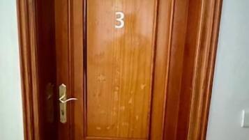 Uma porta de madeira com o número 3, um puxador e um pequeno degrau até o chão.