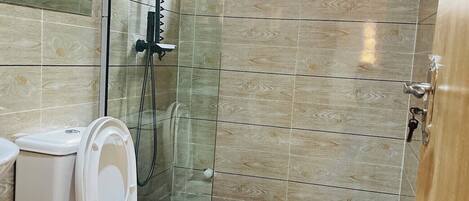 Casa de banho com sanita, chuveiro e uma pequena janela.