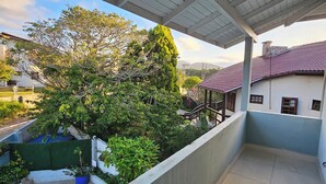 Varanda coberta com vista para uma piscina, uma árvore e um edifício com telhado vermelho.