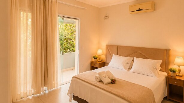 Quarto de hotel com cama, mesa de cabeceira, luminária, janela com cortinas e luz no teto.