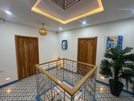 Quarto com mesa de vidro central, portas de madeira, planta em vaso e ladrilhos estampados.