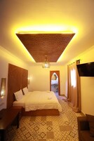 Quarto de hotel com cama, escrivaninha, televisão e piso estampado.