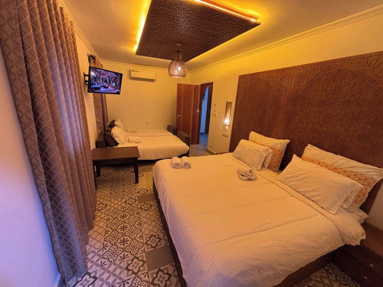 Quarto de hotel com duas camas, uma televisão e piso estampado.
