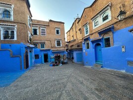 Uma rua estreita com edifícios pintados em azul e bege, que leva a uma pequena loja ao fundo.
