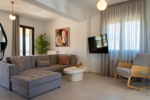 Uma sala de estar moderna com um sofá seccional, uma mesa de centro redonda, uma televisão e uma poltrona de vime.
