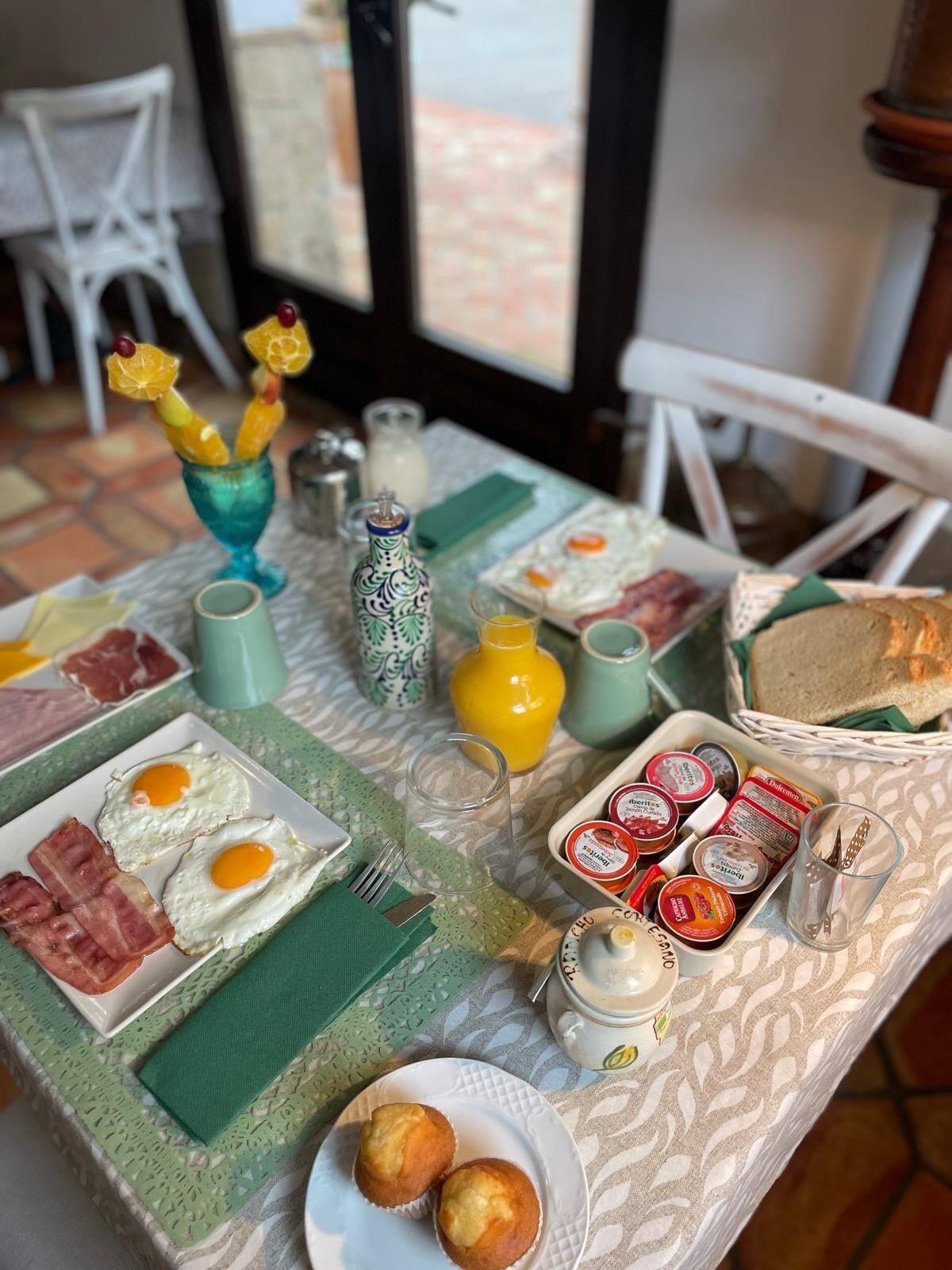 Uma mesa de café da manhã com ovos, bacon, muffins e diversos acompanhamentos.