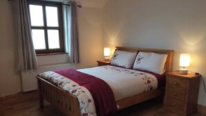 Quarto com cama de madeira, duas mesas de cabeceira com abajures, janela com cortinas e radiador.