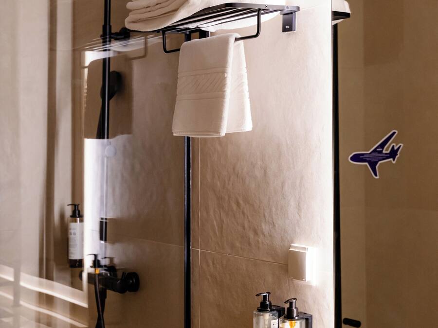 Um banheiro moderno com box de vidro, porta-toalhas com toalhas dobradas e itens de higiene em uma prateleira.