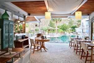 Área de refeições interna com vista para a piscina, móveis de madeira e teto coberto.