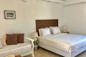 Quarto de hotel com cama, mesa de cabeceira com abajur e sofá.