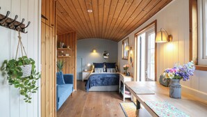 Um quarto aconchegante com teto de madeira, cama com roupa de cama azul, mesas de cabeceira, uma escrivaninha pequena e uma cadeira.