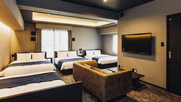 Quarto de hotel com duas camas, um sofá, uma televisão e uma luminária no teto.