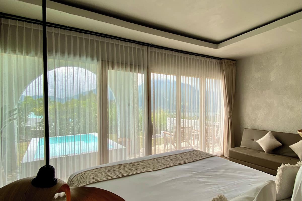 Quarto de hotel moderno com uma cama grande, vista para uma piscina e varanda.