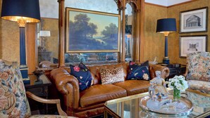 Uma sala de estar luxuosa com um sofá de couro marrom, poltronas florais e uma mesa de centro de vidro.