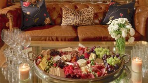 Quarto luxuoso com sofá de couro, espelho decorativo e bandeja com queijos e frutas variados.
