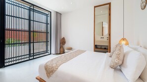 Quarto com cama grande, espelho com moldura de madeira, mesa de cabeceira e vista através de uma porta deslizante.