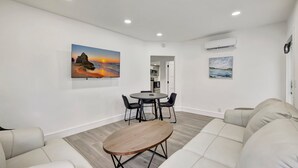 Uma sala de estar moderna com um sofá, uma mesa de centro de madeira, uma mesa de jantar com cadeiras e obras de arte nas paredes.