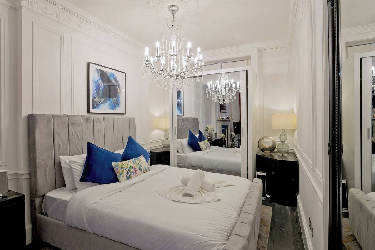 Quarto de hotel com uma cama grande, um candelabro, um espelho e um quadro na parede.