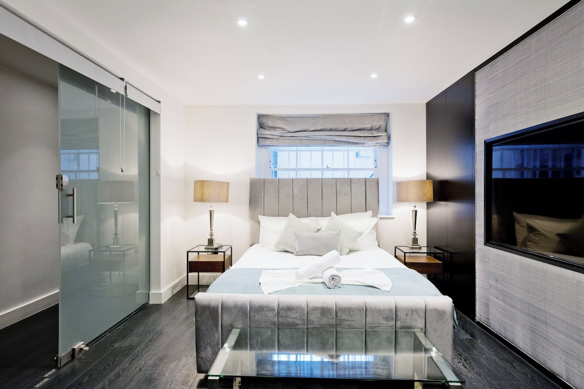 Quarto moderno com cama grande, divisória de vidro e vista para a cidade.