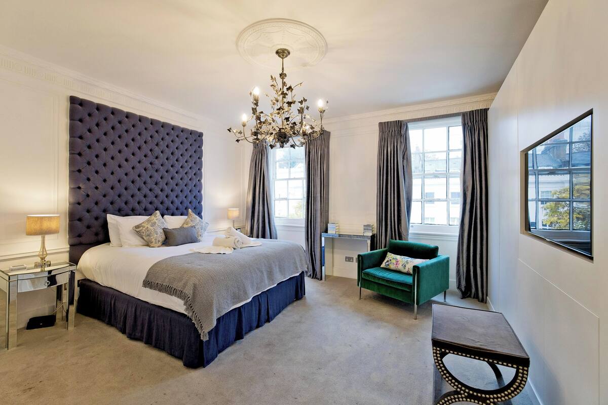 Quarto com uma cama grande, um lustre, uma poltrona verde e uma escrivaninha.