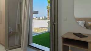 Quarto de hotel com porta de vidro deslizante que dá para uma varanda com vista para edifícios e uma palmeira.