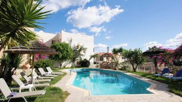 Piscina com espreguiçadeiras, estrutura de telhado de palha e vegetação ao redor.