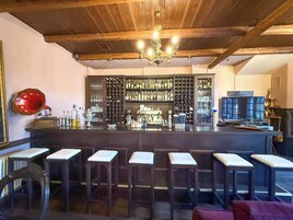 Uma área de bar com teto de madeira, um candelabro e um suporte para vinhos. Há banquetas e uma televisão.